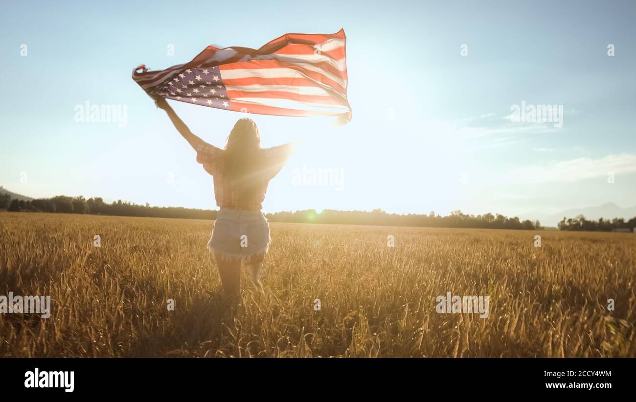 Young woman waves an american flag on the wheat field. Patriotic ...