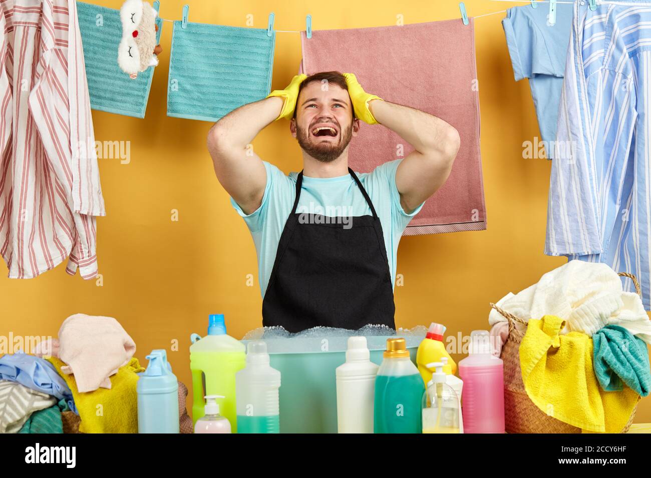 Overwhelmed angry young man with apron and gloves holding hands on head ...