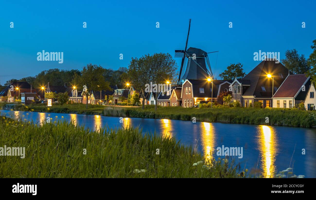 Typical traditional dutch village with farms and windmill along canal ...