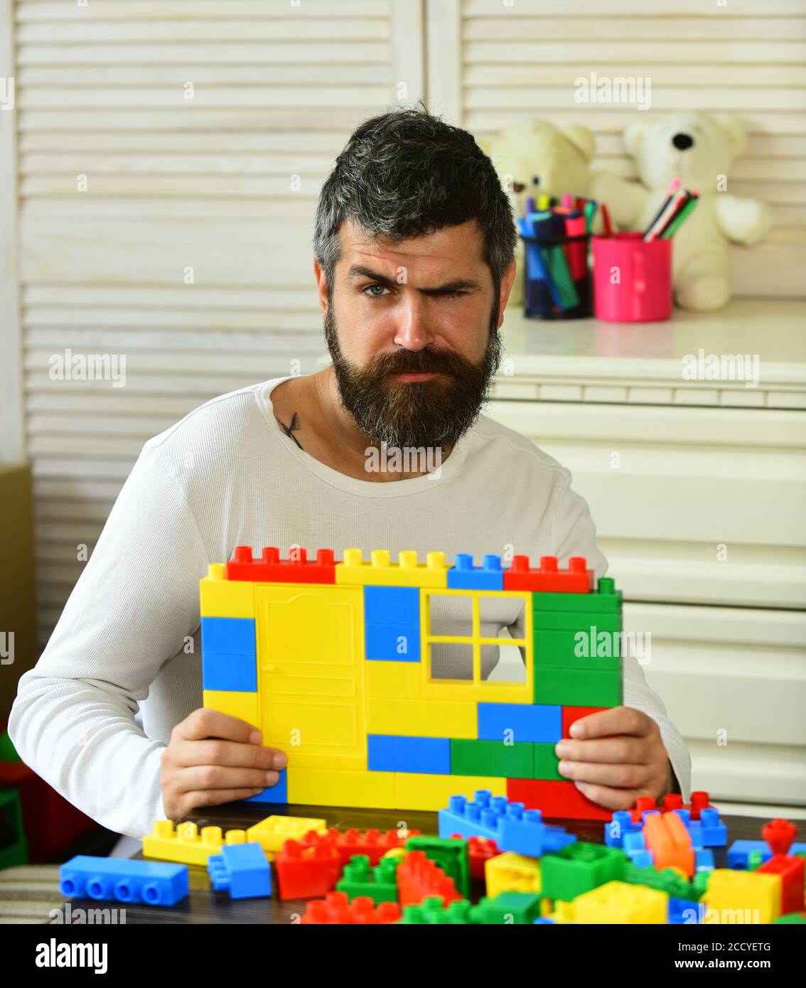 Man with concerned face makes brick constructions for kids. Toys and ...
