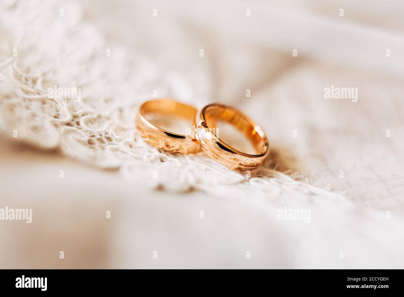 Two gold wedding rings for the bride and groom with a gem on white lace ...