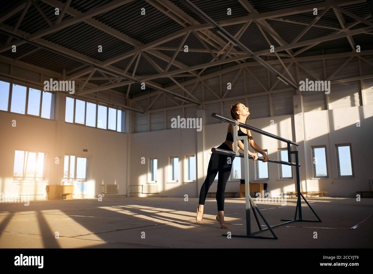 Pleasant young female athlete training at ballet bar, standing on ...