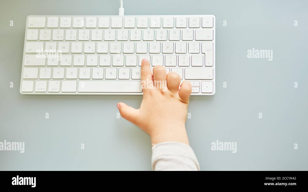 Little child is typing on the computer keyboard with his index finger ...