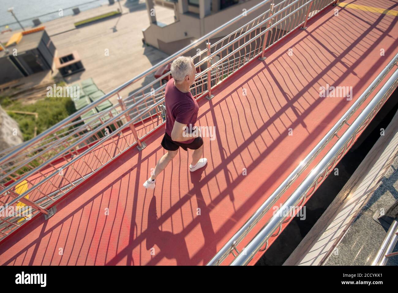 Mature grey-haired male running across the bridge Stock Photo - Alamy