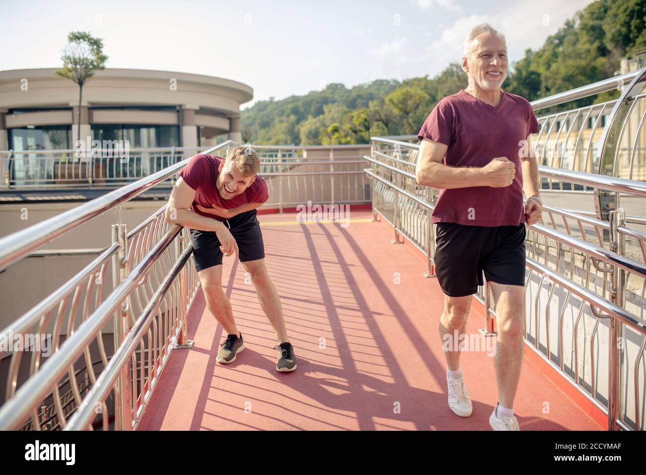 Grey-haired male jogging across bridge, young male holding hand on his ...
