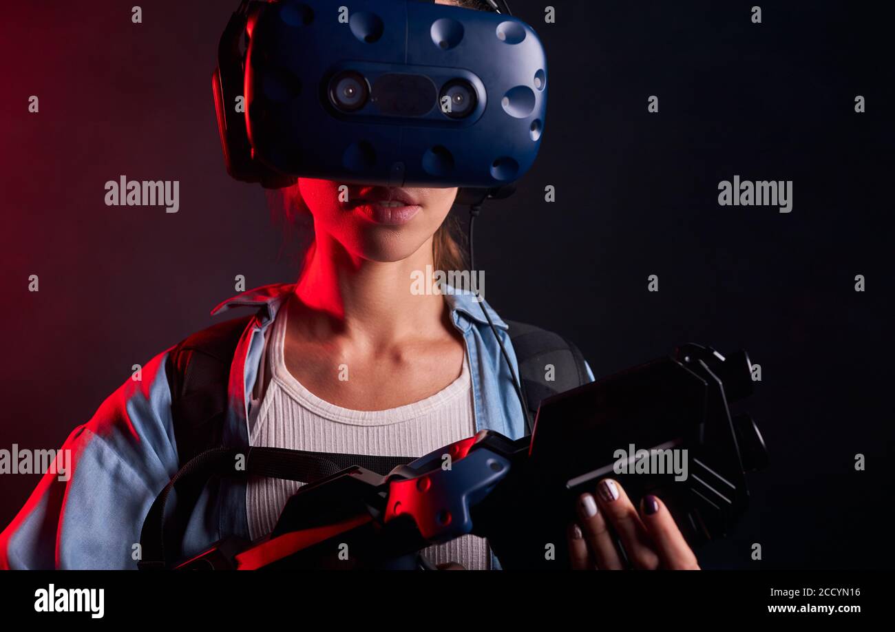 Young caucasian woman holding shooter VR, wearing eye mask, stand ...