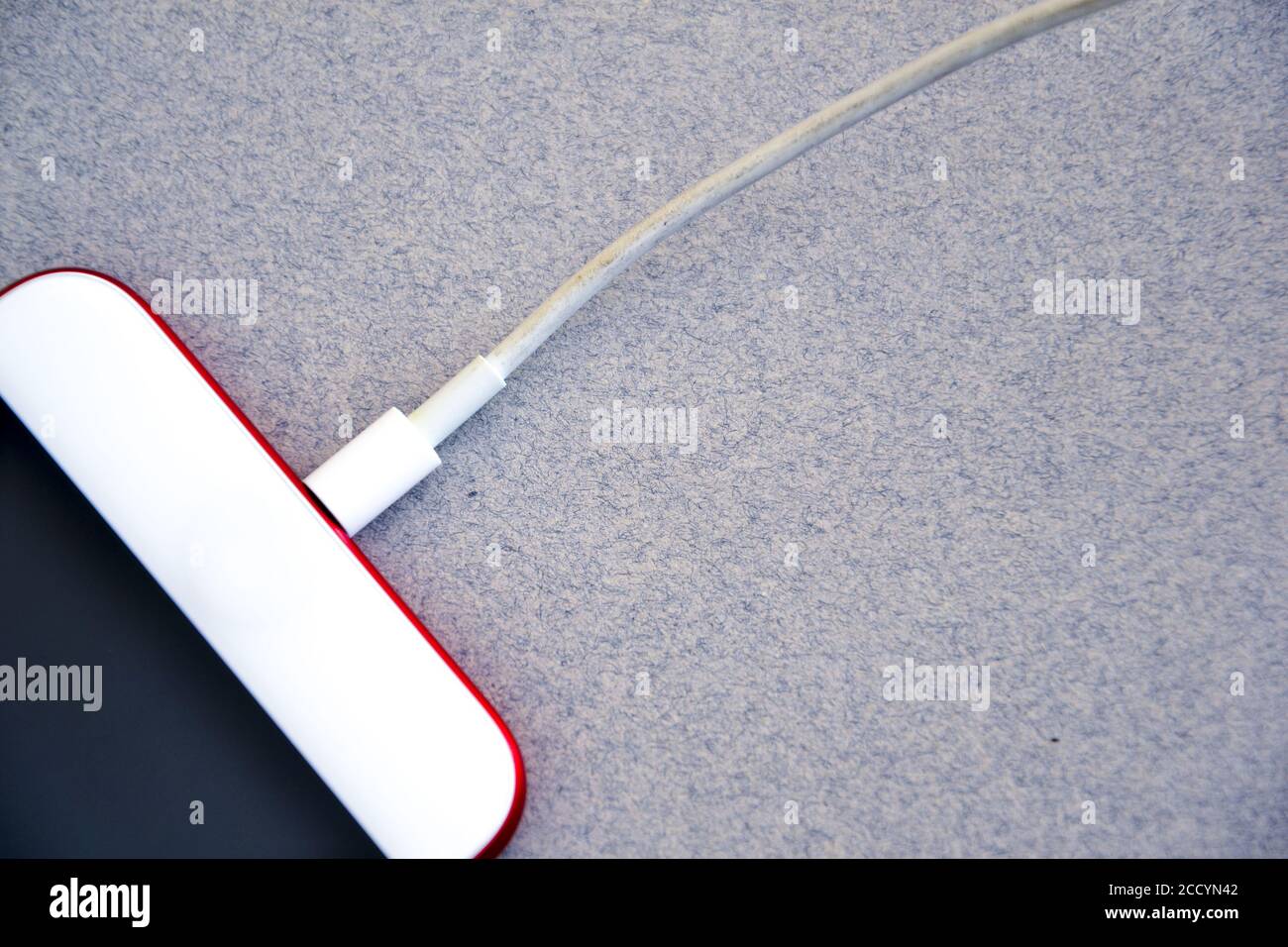 Closeup shot of a smartphone with a charger cable on a gray surface ...