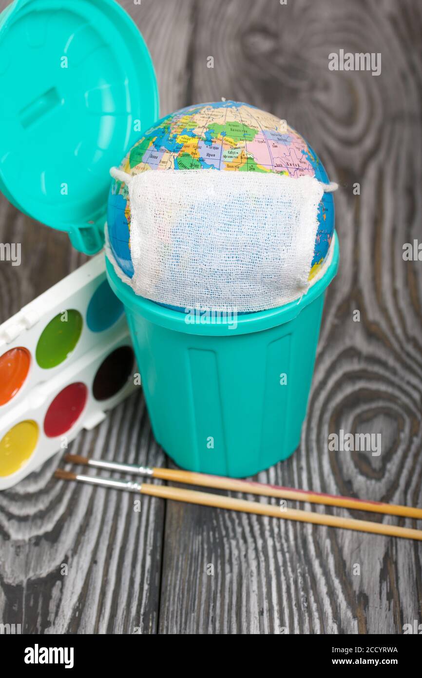 Globe with medical mask. Lies in a trash can. Nearby watercolors and ...