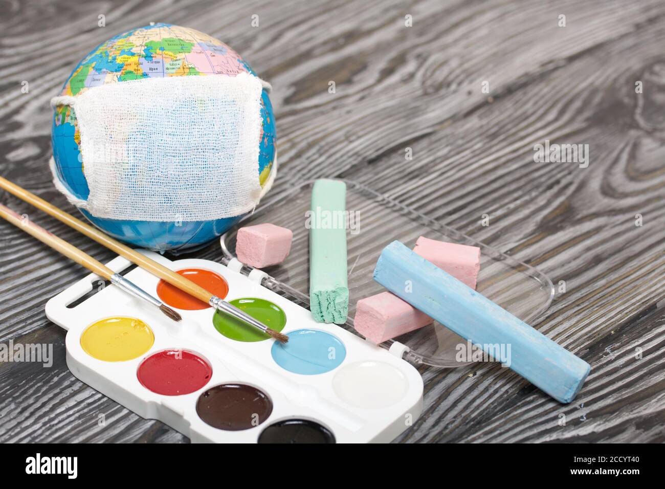 Globe with medical mask. Nearby are crayons and watercolors. Academic ...