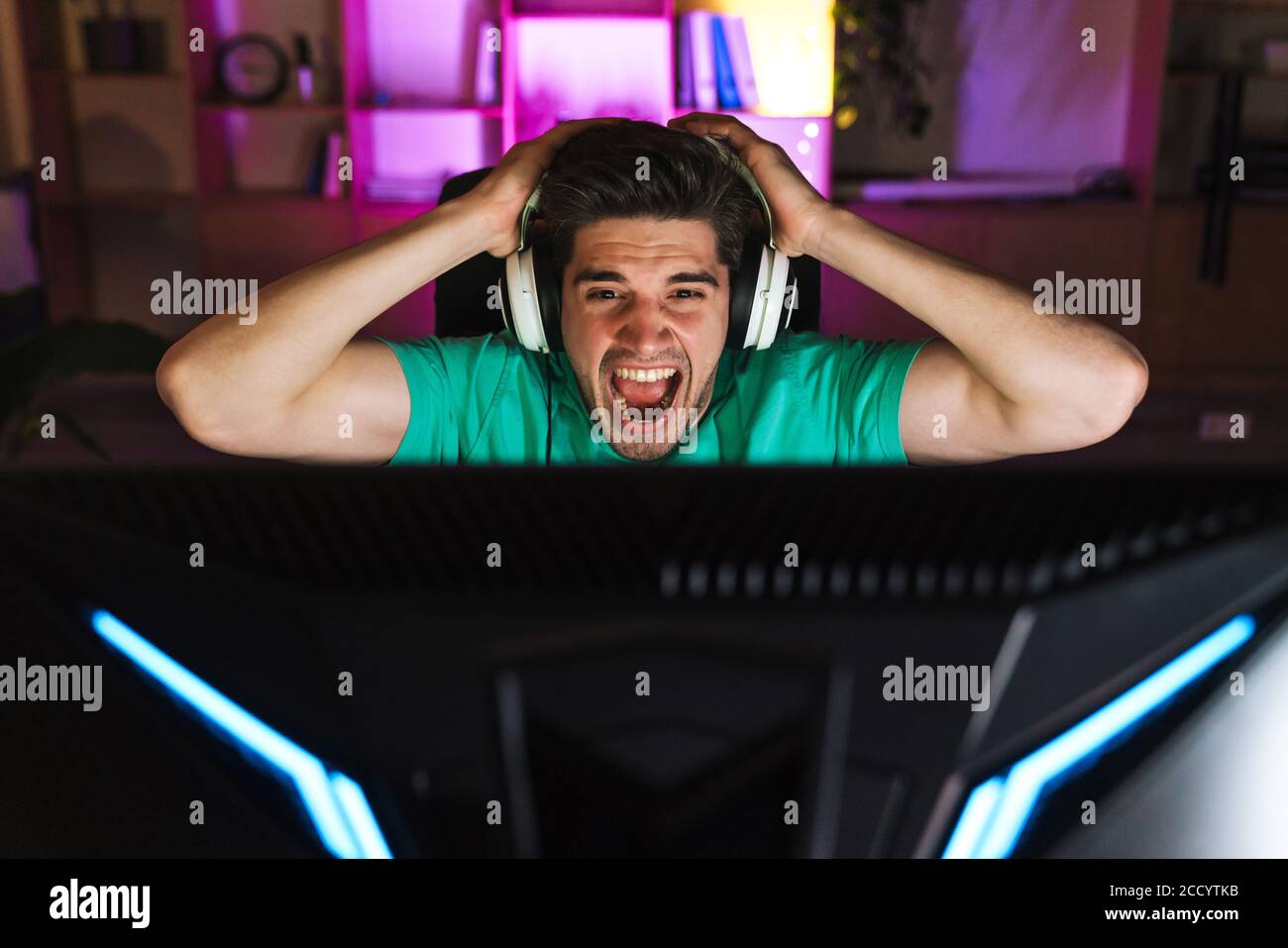 Image of unhappy young man in headphones grabbing his head while ...