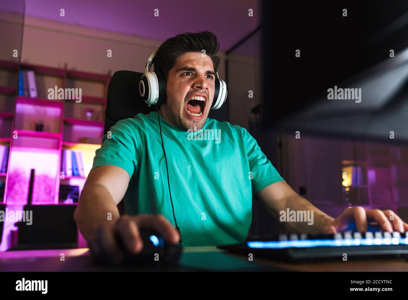 Image of shocked young man in headphones screaming while playing video ...