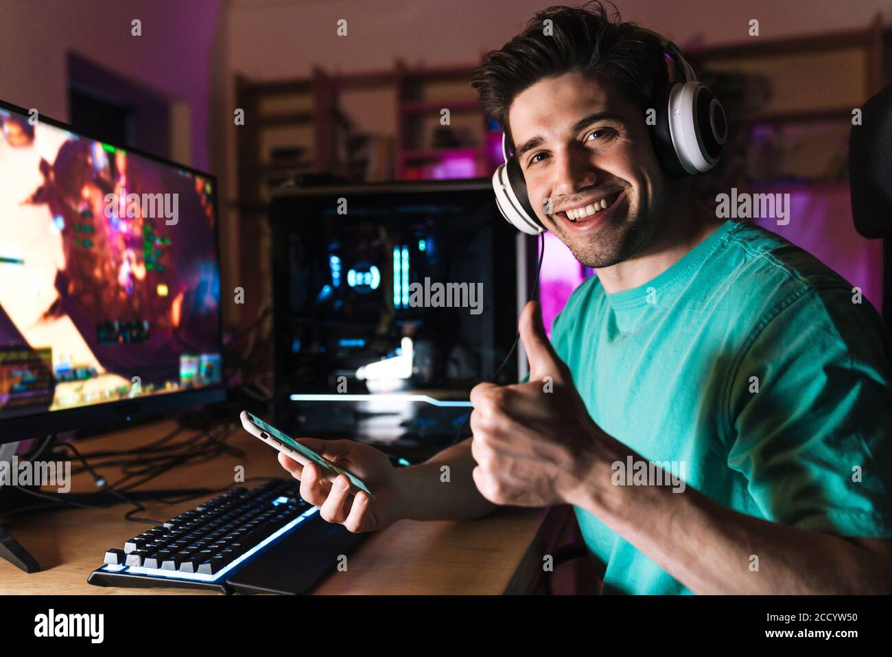 Image of joyful man showing thumb up and using cellphone while playing ...