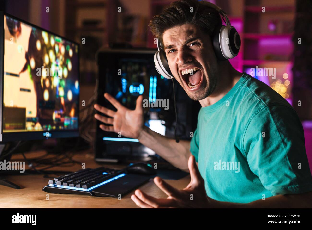 Image of furious young man in headphones screaming while playing video ...