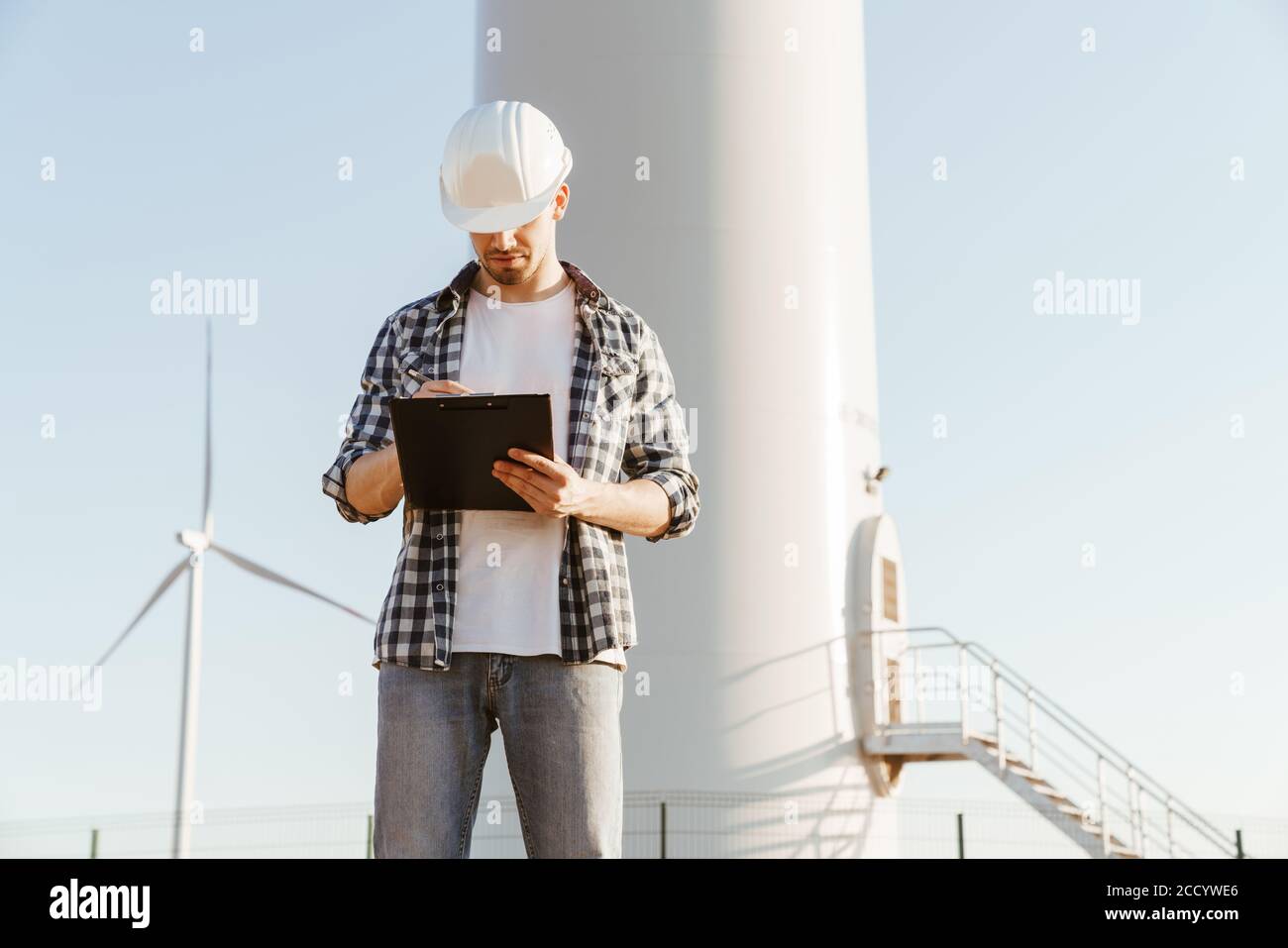 An electrical engineer standing on a field with windmills, taking notes ...
