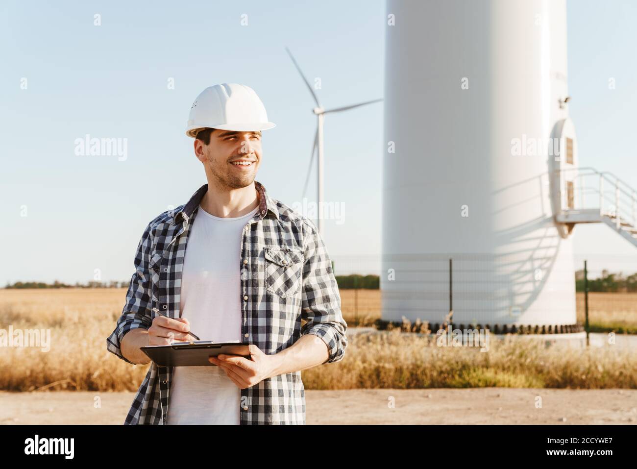 A smiling electrical engineer standing on a field with windmills ...