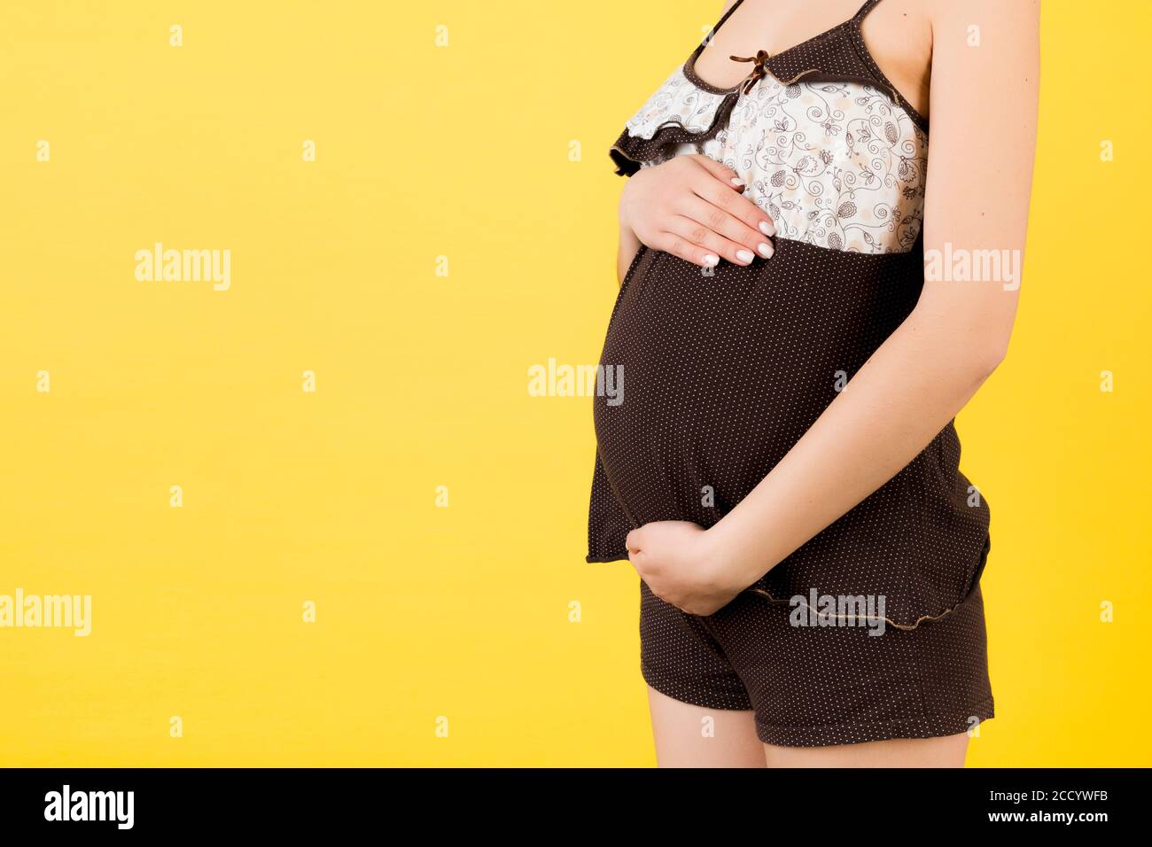 Cropped image of pregnant woman in brown pajamas touching her belly at ...