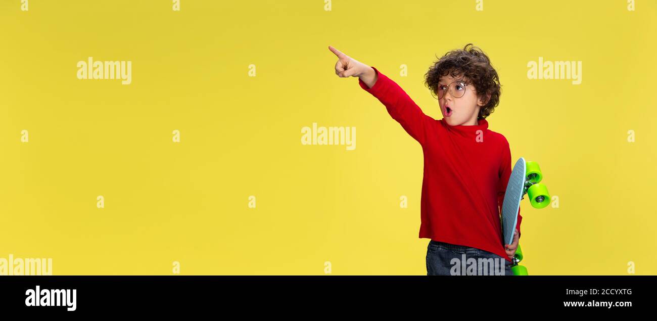 Pointing. Portrait of pretty young curly boy in red wear on yellow ...