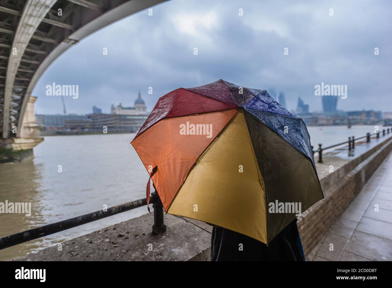 A tourist looks to the city of London as they shelter under a colourful ...