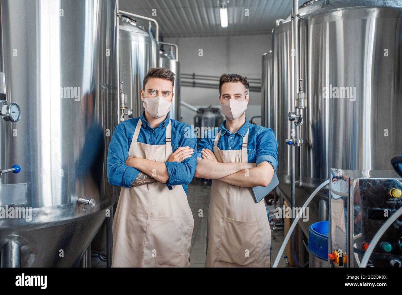 Handsome owners of brewery in masks and aprons, near brewing kettles ...