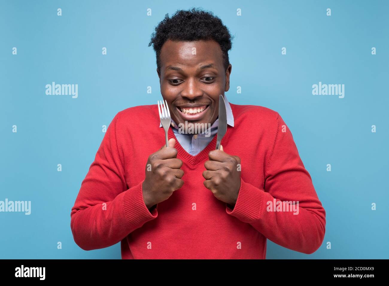 Hungry african man holding fork and knife raised waiting for dinner ...