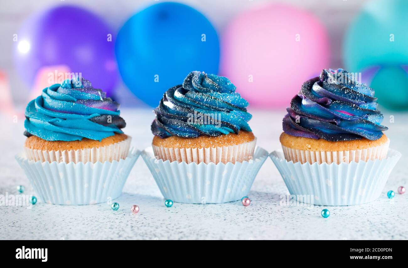 Three vanilla cupcakes with galaxy blue whipped cream on party ...