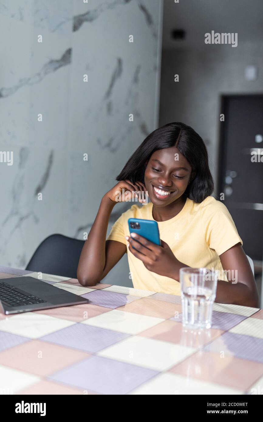 Young african woman use phone, while sitting in kichten Stock Photo - Alamy
