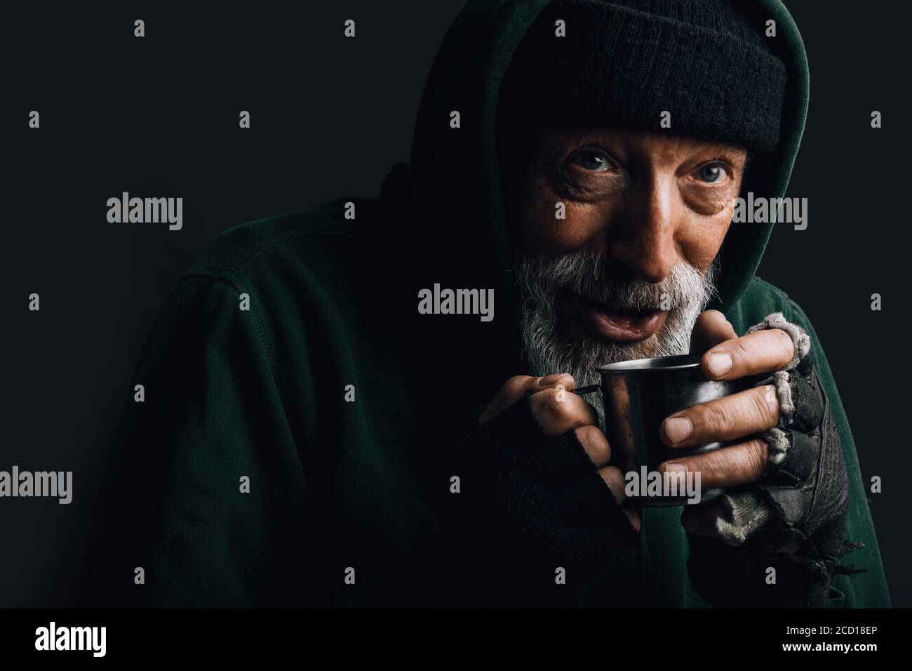 Old homeless man with grey beard covering up in green decrepit wear ...