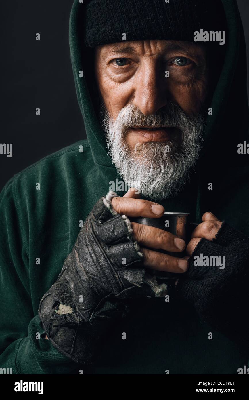 Old homeless man with grey beard covering up in green decrepit wear ...