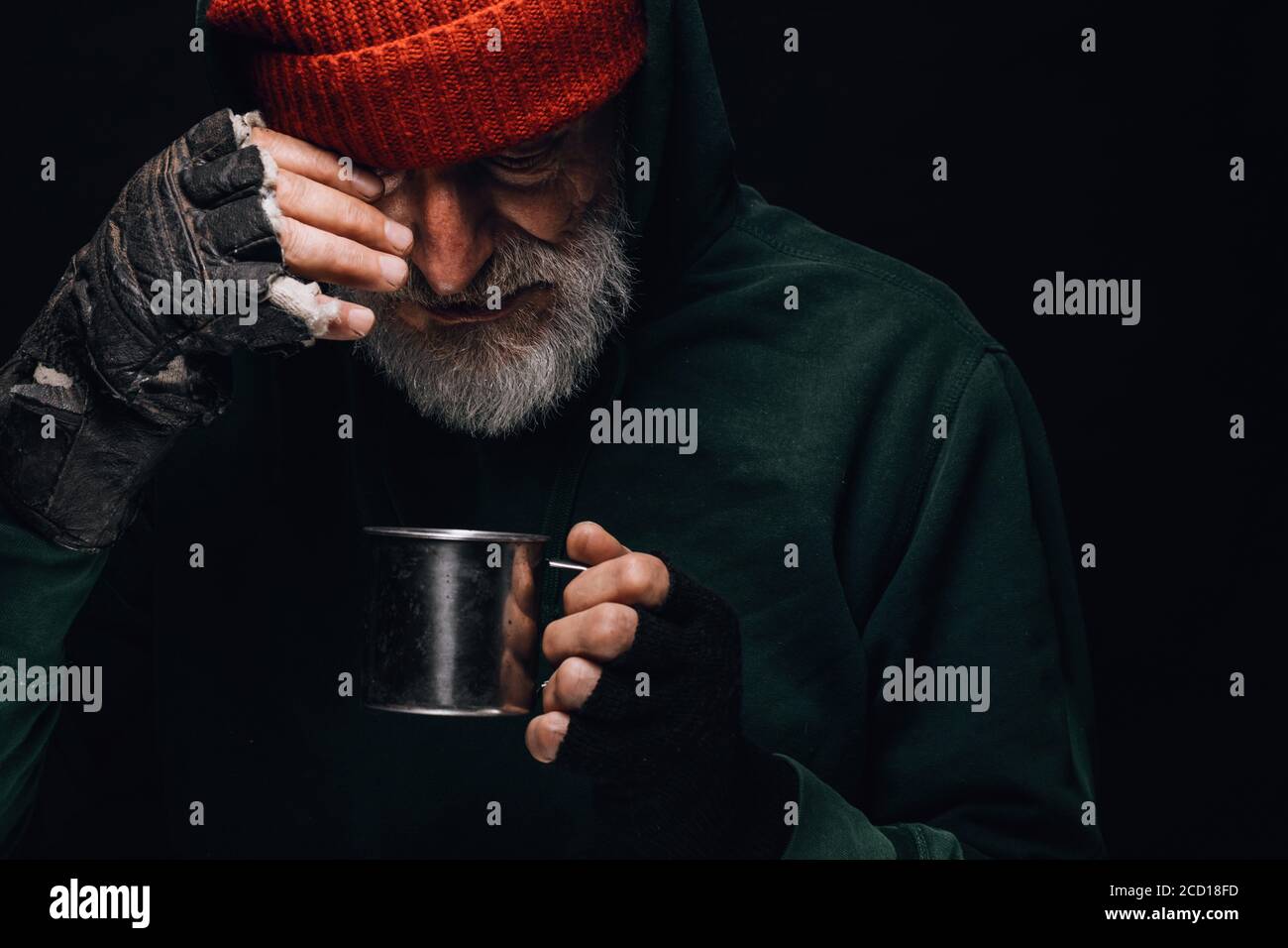 Old homeless man with grey beard covering up in green decrepit clothes ...
