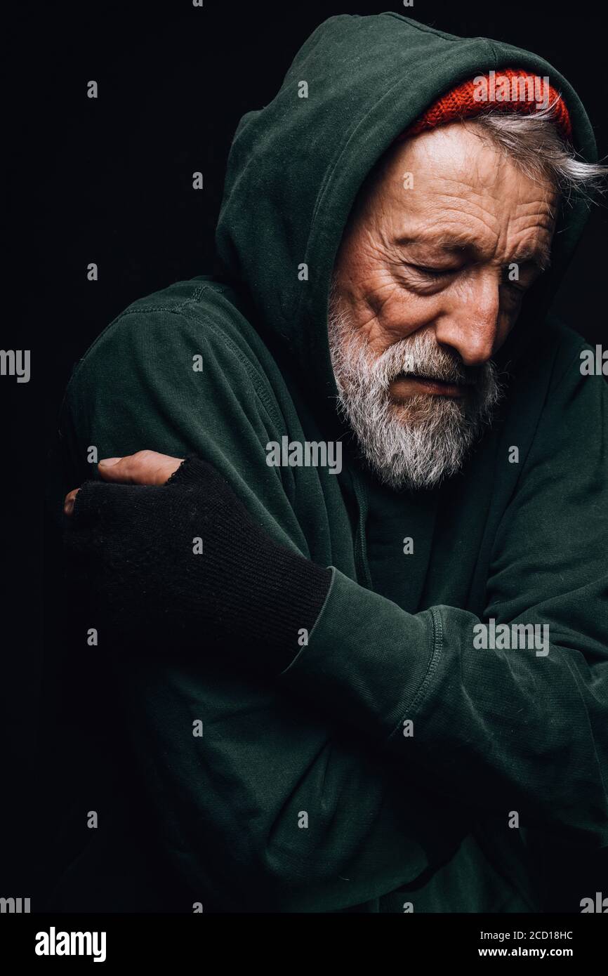 Old grey-bearded frozen tramp man with grey beard embracing himself to ...
