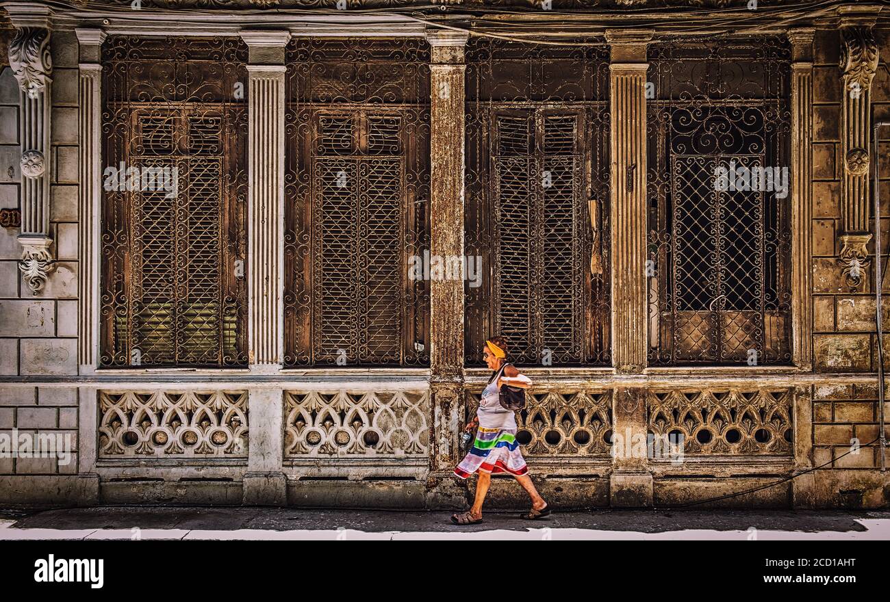 Havana, Cuba, July 2019, woman walking pass a building with windows ...