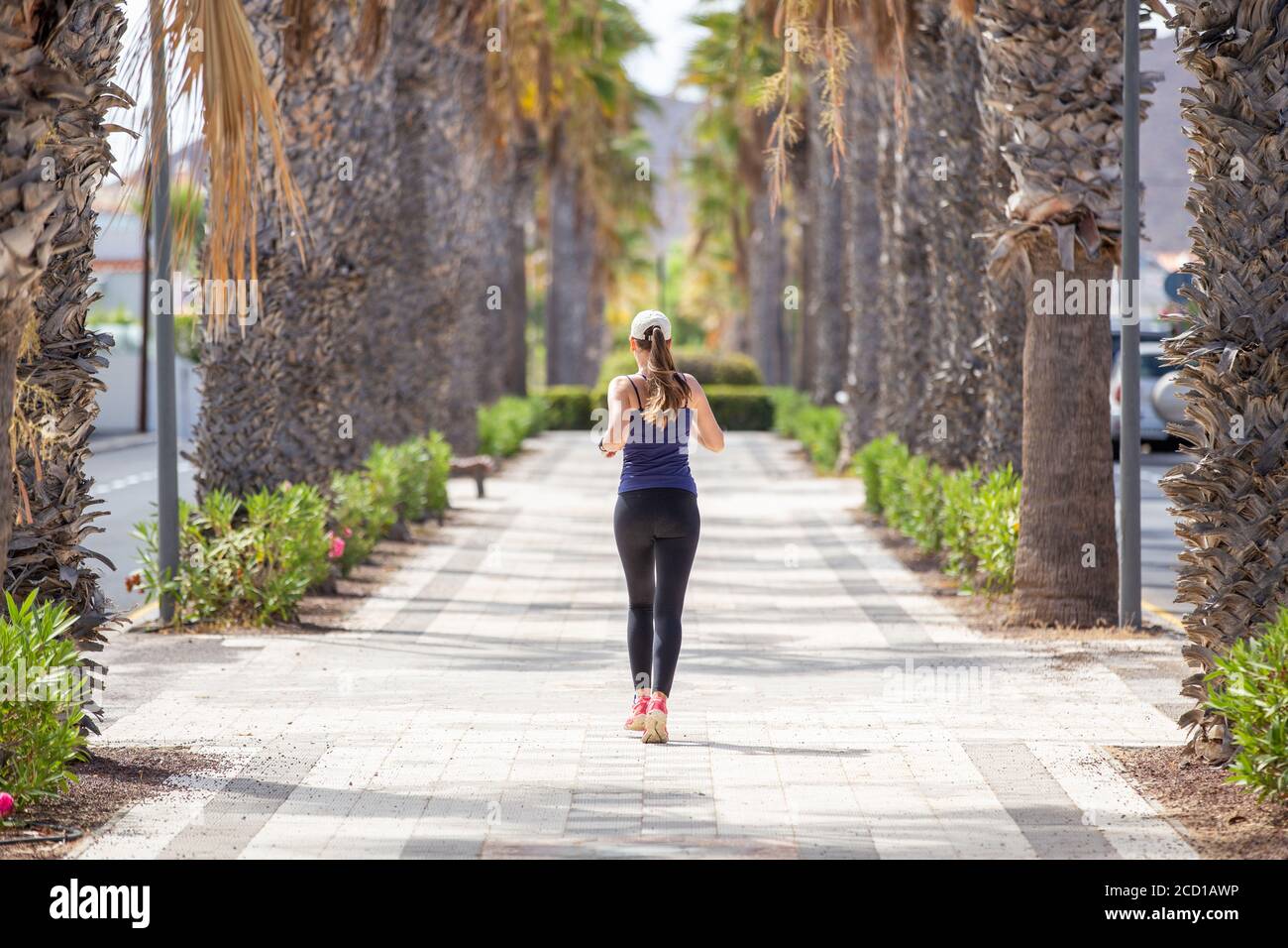 Back view of jogging woman on the street of tropical town. Running girl ...