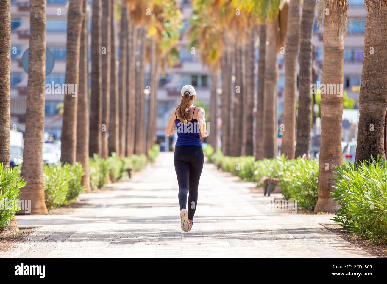Back view of jogging woman on the street of tropical town. Running girl ...