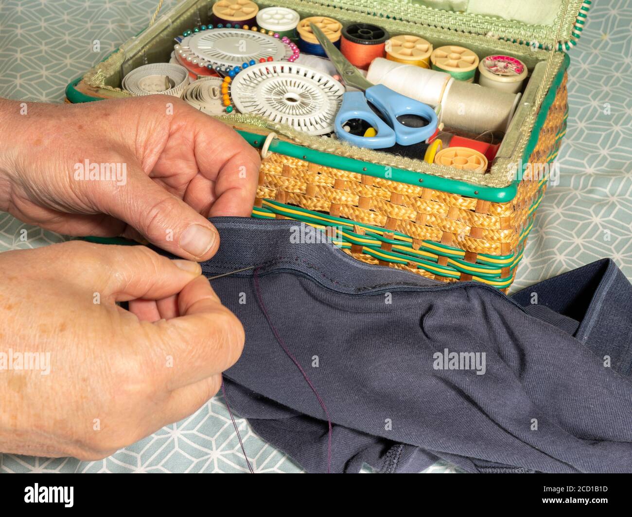 Man’s hands using a needle to sew a pair of underpants with damaged ...