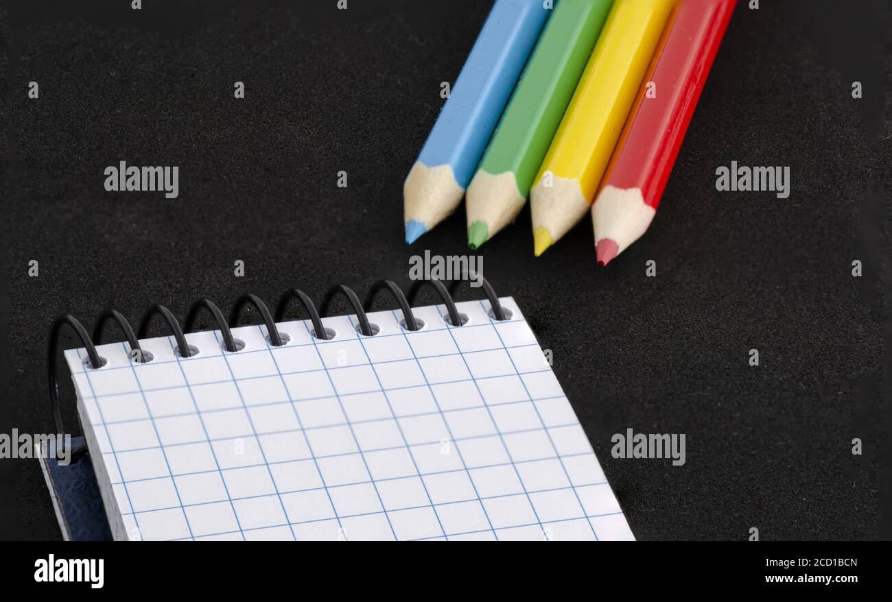 Closeup shot of a gridded notebook with colored pencils on a black ...