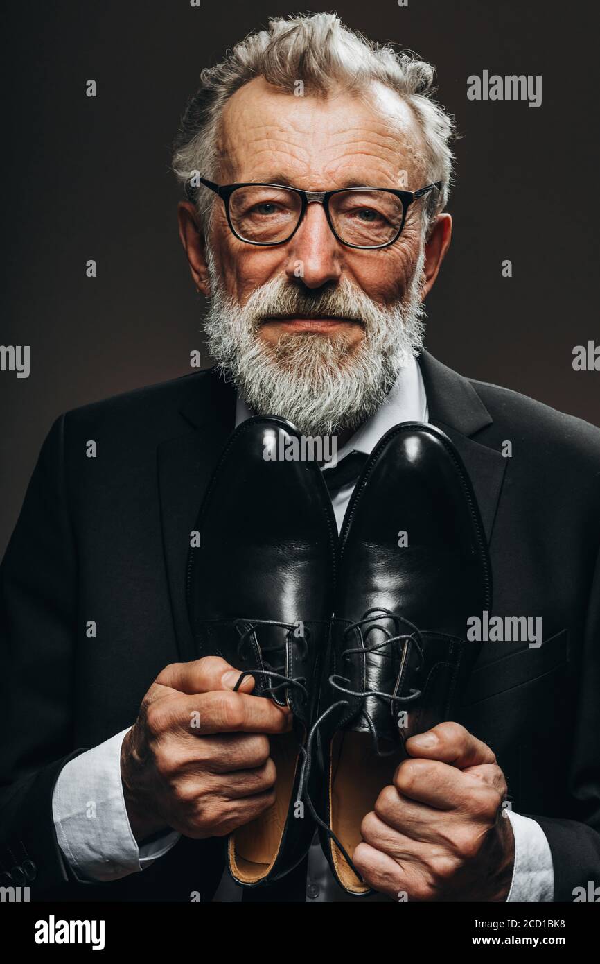 Senior bearded citizen in custom made black suit holding bespoke shoes ...