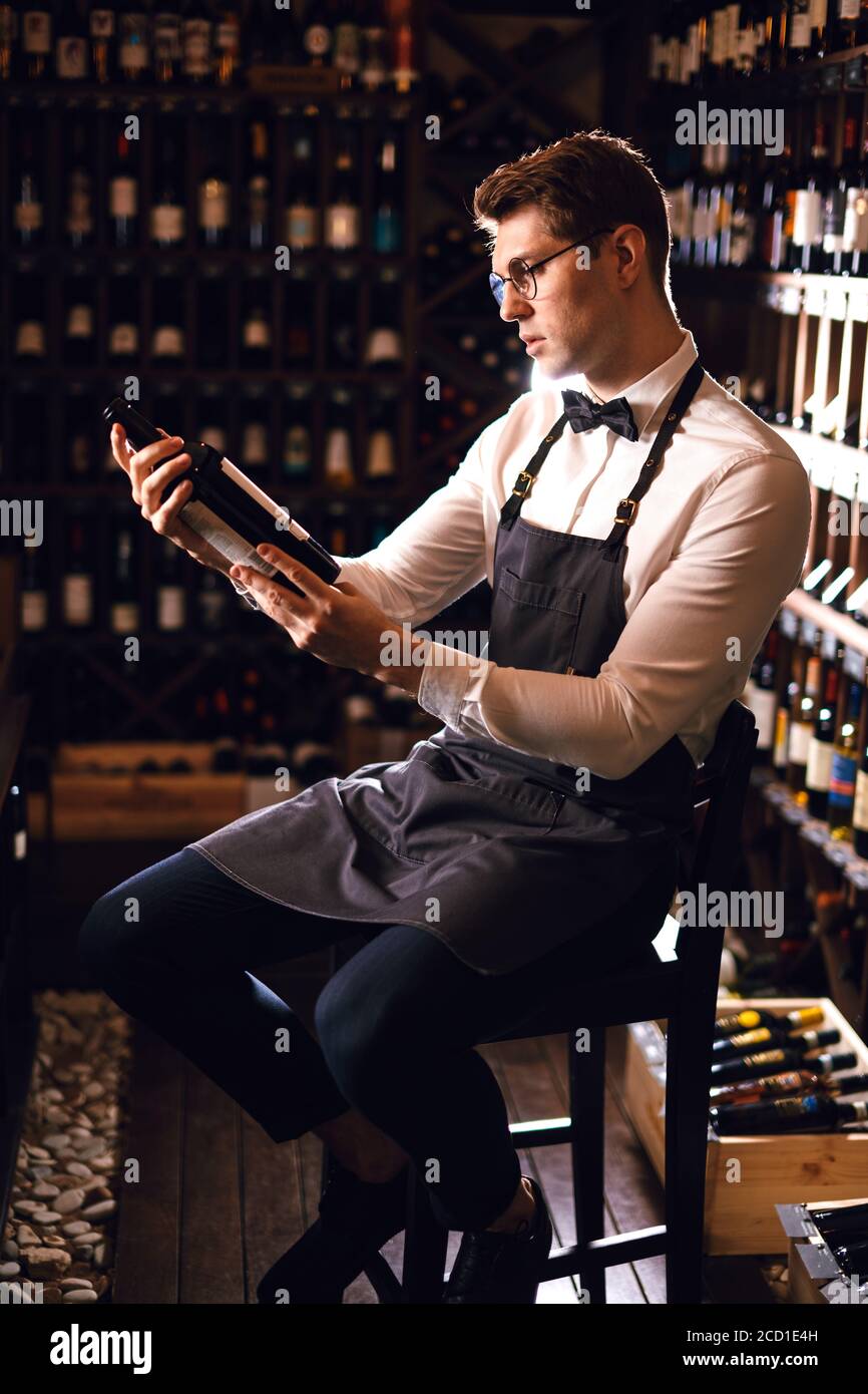 Handsome and young smiling brown haired sommelier with a bottle of wine ...