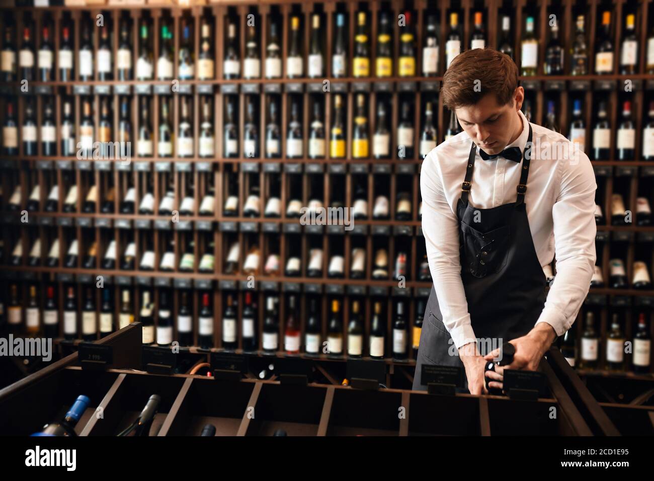 Handsome and young smiling brown haired sommelier with a bottle of wine ...