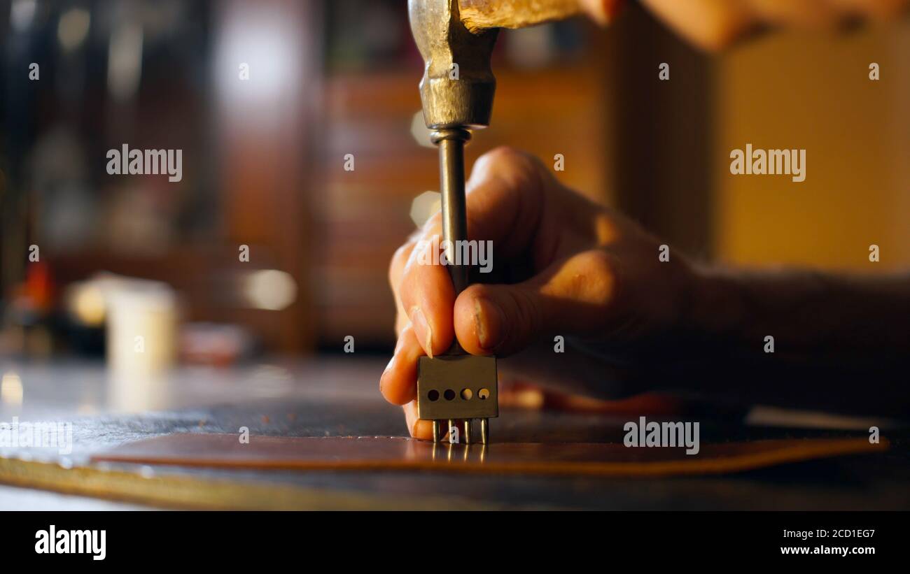 Tanner makes hole in workpiece. Male hands close up holding tool ...