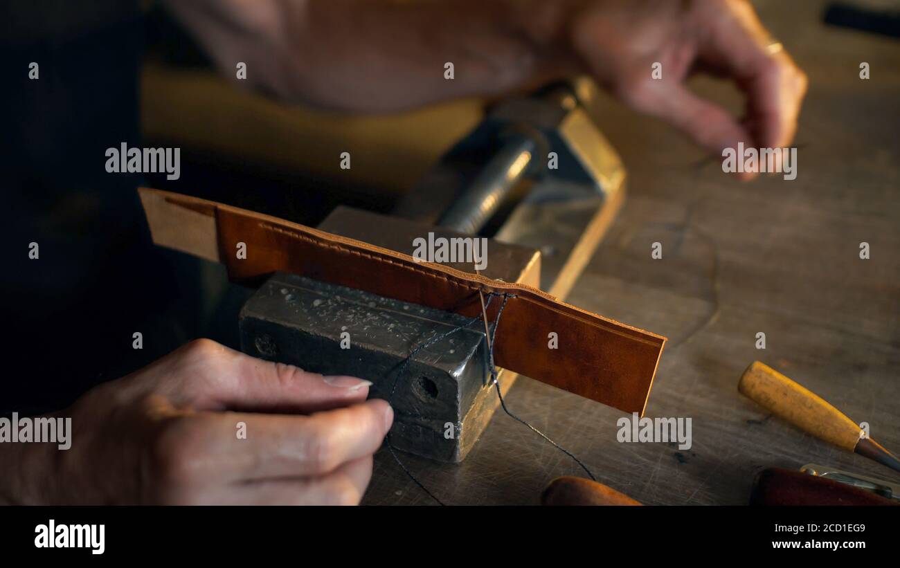 Man sews leather details clamped in vice. Craftsman works with needle ...