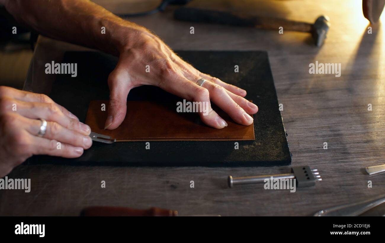 Working process of leather item in workshop. Man holding crafting tool ...