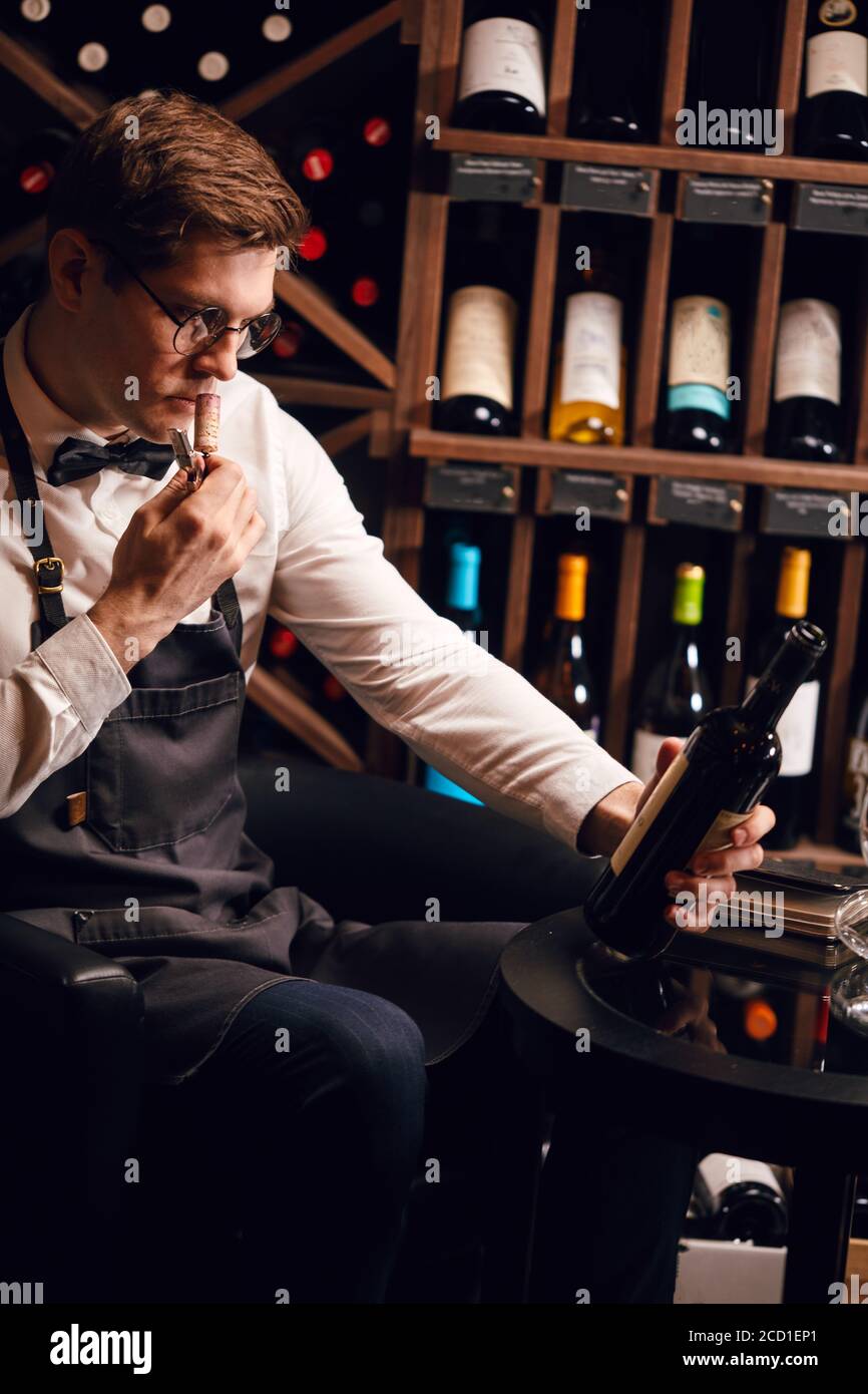 Bartender opens a wine bottle with corkscrew and sniffing the cork ...