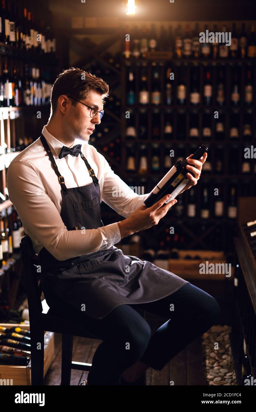 Elegant wine seller holding a bottle of wine and reading label in a ...