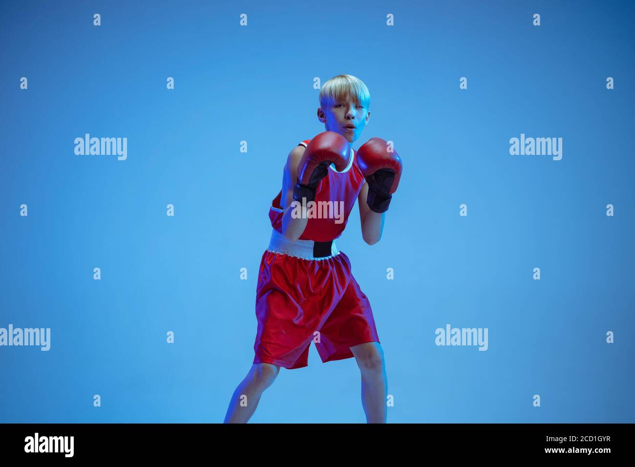Teenager in sportswear boxing isolated on blue studio background in ...