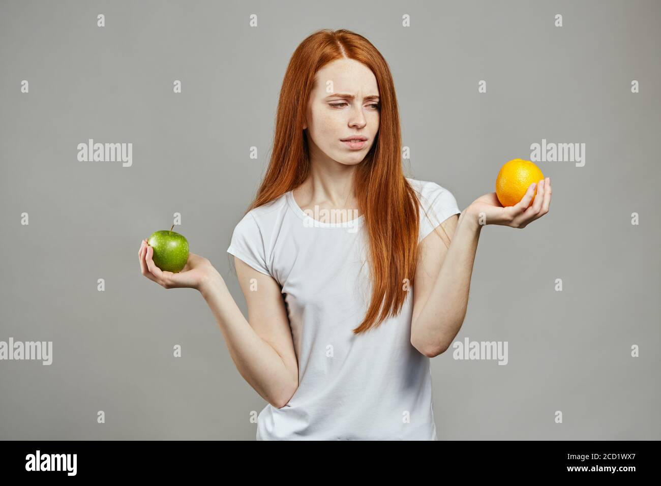 difficult choice. sceptical girl holding an apple and an orange. close ...