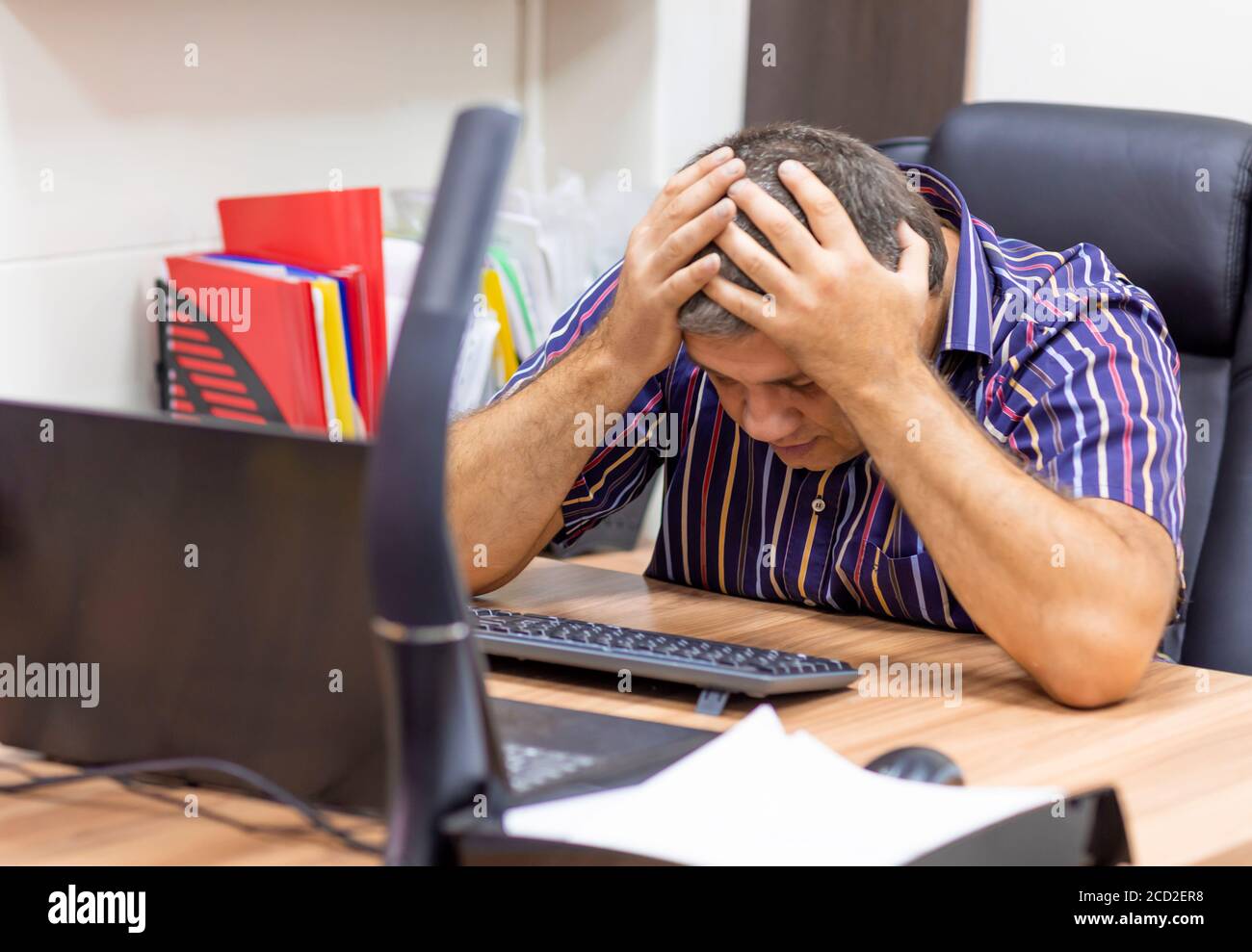 Frustrated man in front of the monitor covered his head with his hands ...