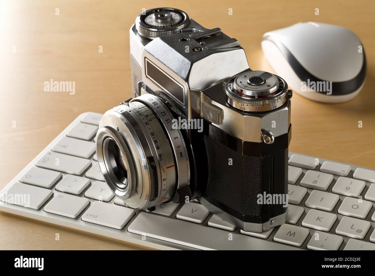 Retro analog SLR camera on top of computer keyboard and mouse on wooden ...
