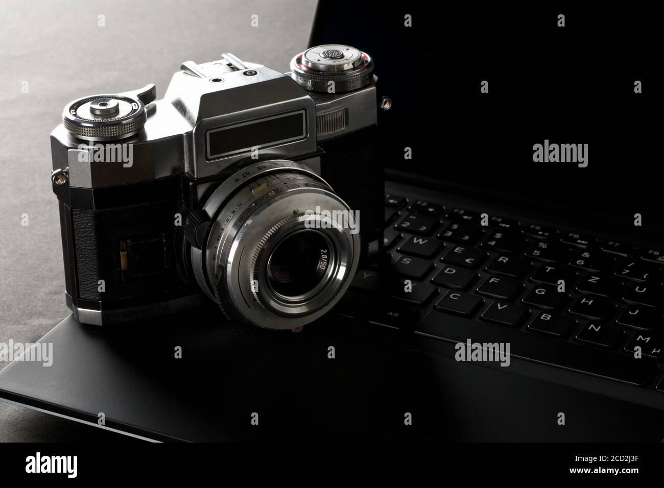Retro analog SLR camera on laptop keyboard on black desk in office ...