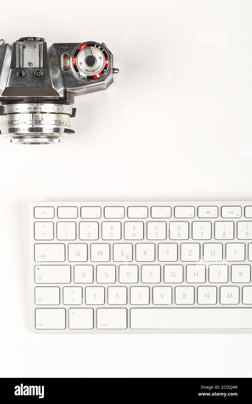 Retro analog SLR camera next to computer keyboard on white background ...