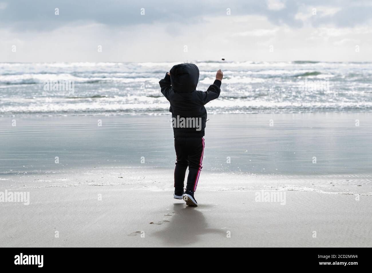 Young boy on the beach throwing a rock into the ocean Stock Photo - Alamy